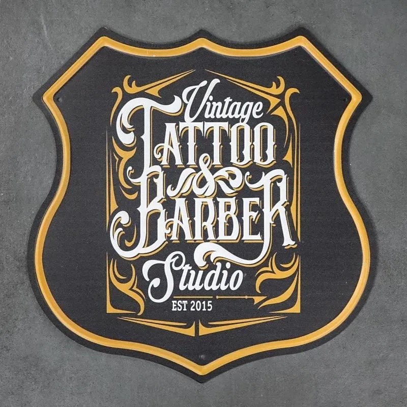 Kovová cedule ve tvaru štítu Tattoo&Barber